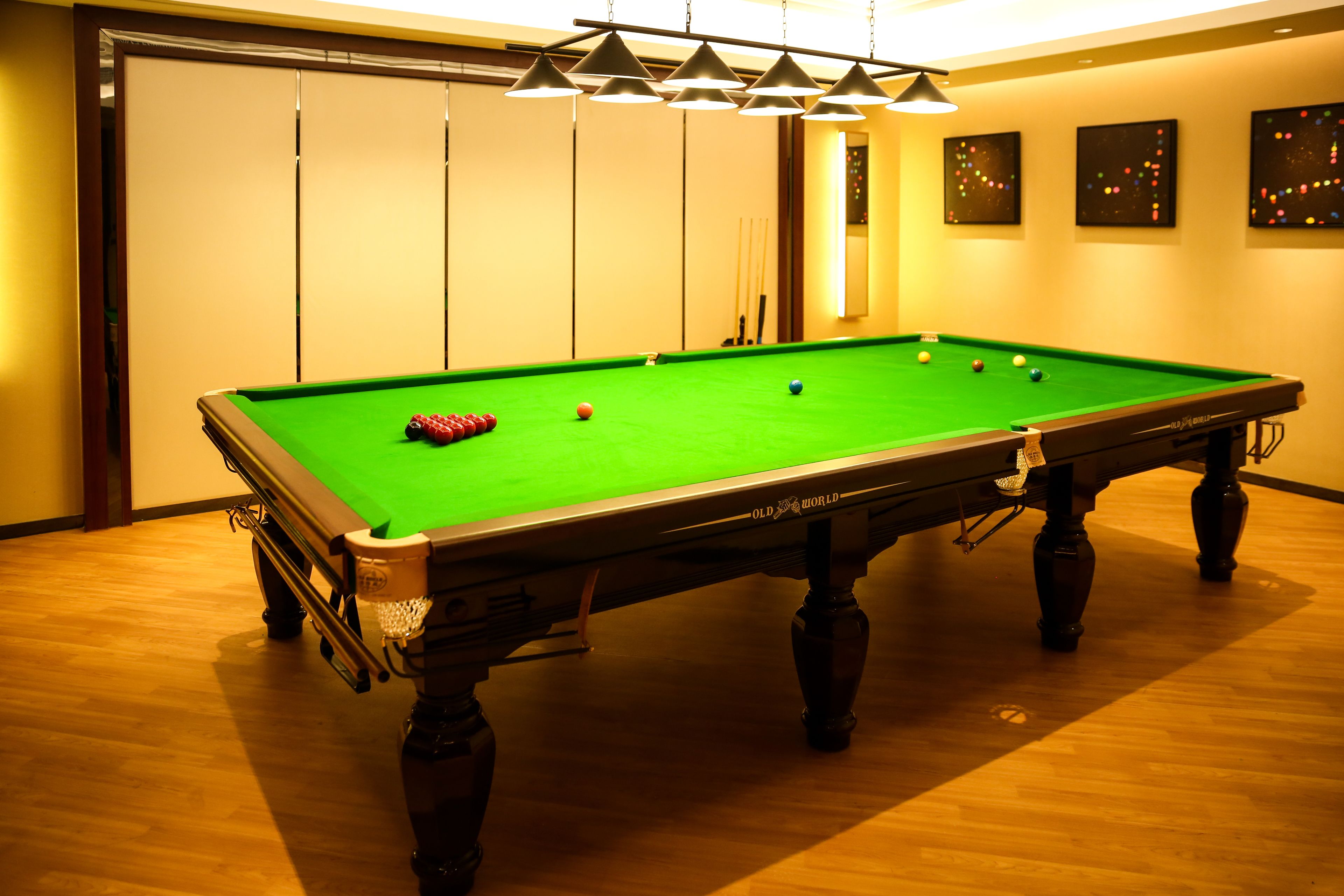 Uma mesa de bilhar com bolas, superfície de feltro verde e piso de madeira.