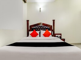 Uma cama bem arrumada com cabeceira de madeira, roupa de cama branca e dois travesseiros vermelhos.