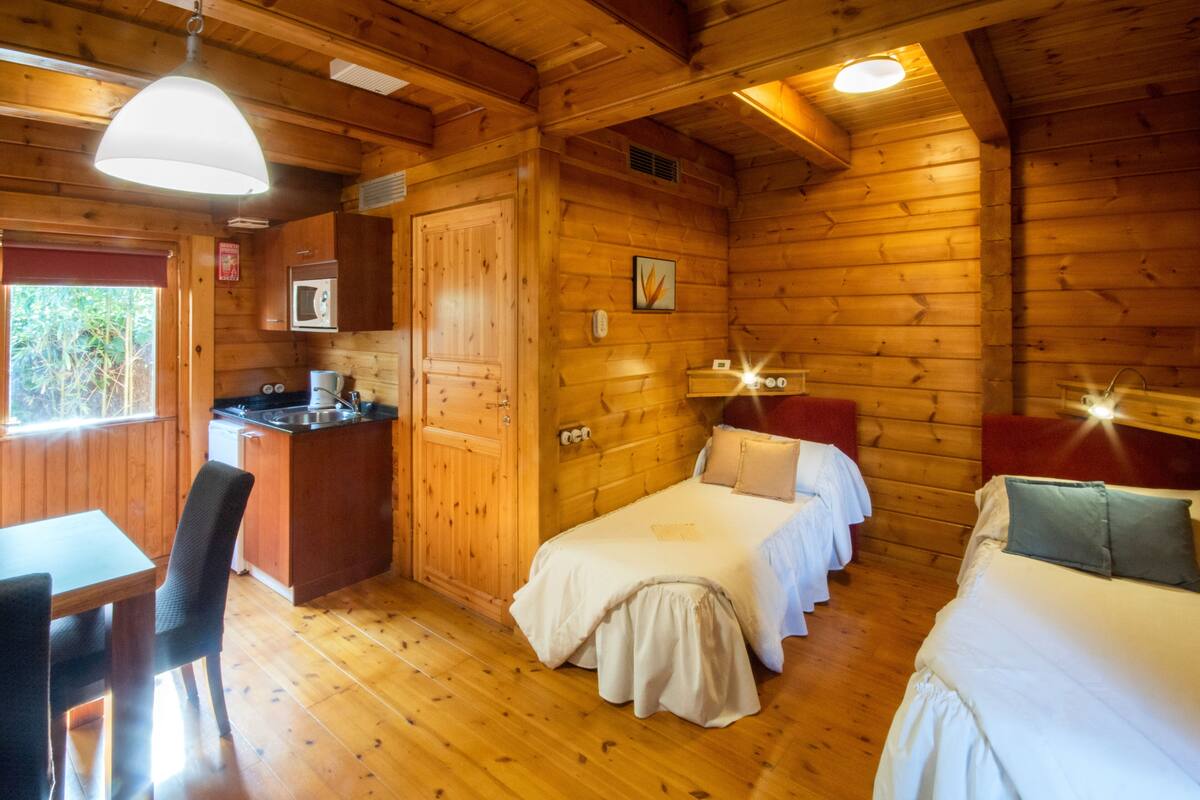 Uma cabana de madeira com cozinha, área de jantar e duas camas.