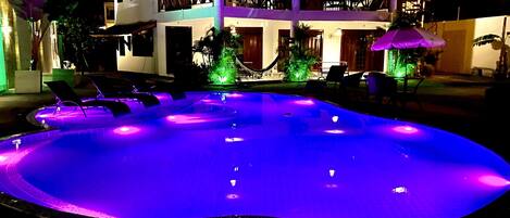 Piscina externa com borda curva, cercada por espreguiçadeiras e guarda-sóis.