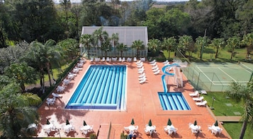 Piscina com espreguiçadeiras próximas e quadra de tênis.