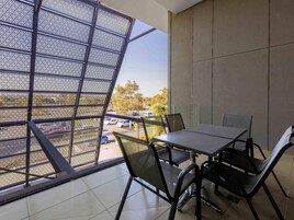 Uma varanda com mesa e cadeiras, vista para um estacionamento e um edifício de design moderno.