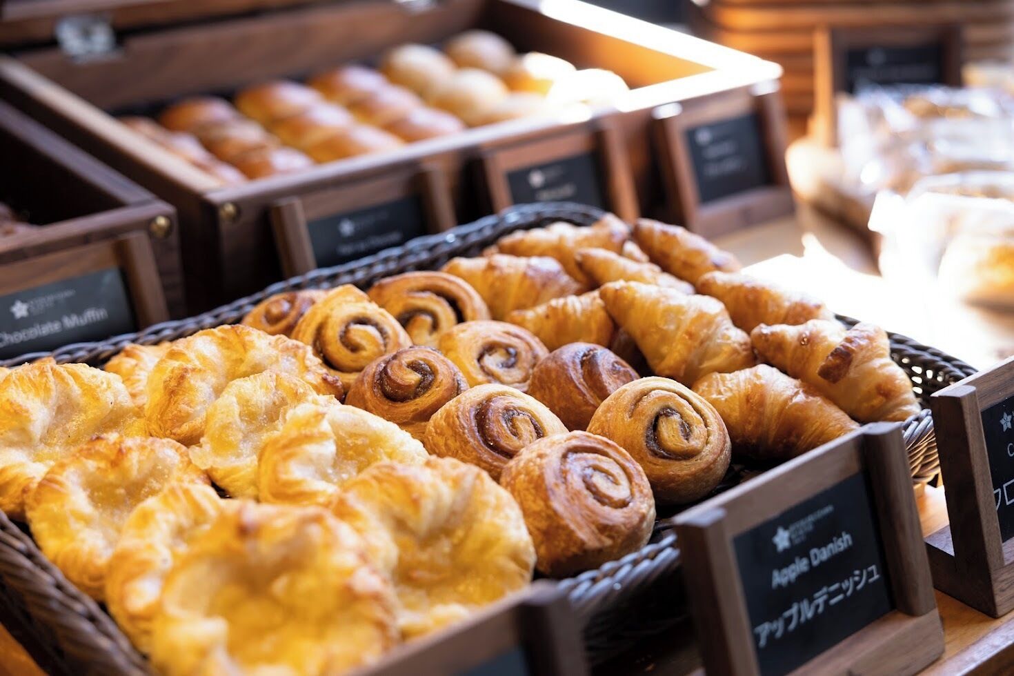 Vitrine de padaria com diversos produtos de panificação, incluindo croissants e muffins, dispostos em caixas de madeira.