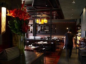 Restaurante com mesas, cadeiras e um bar, e uma pessoa caminhando.