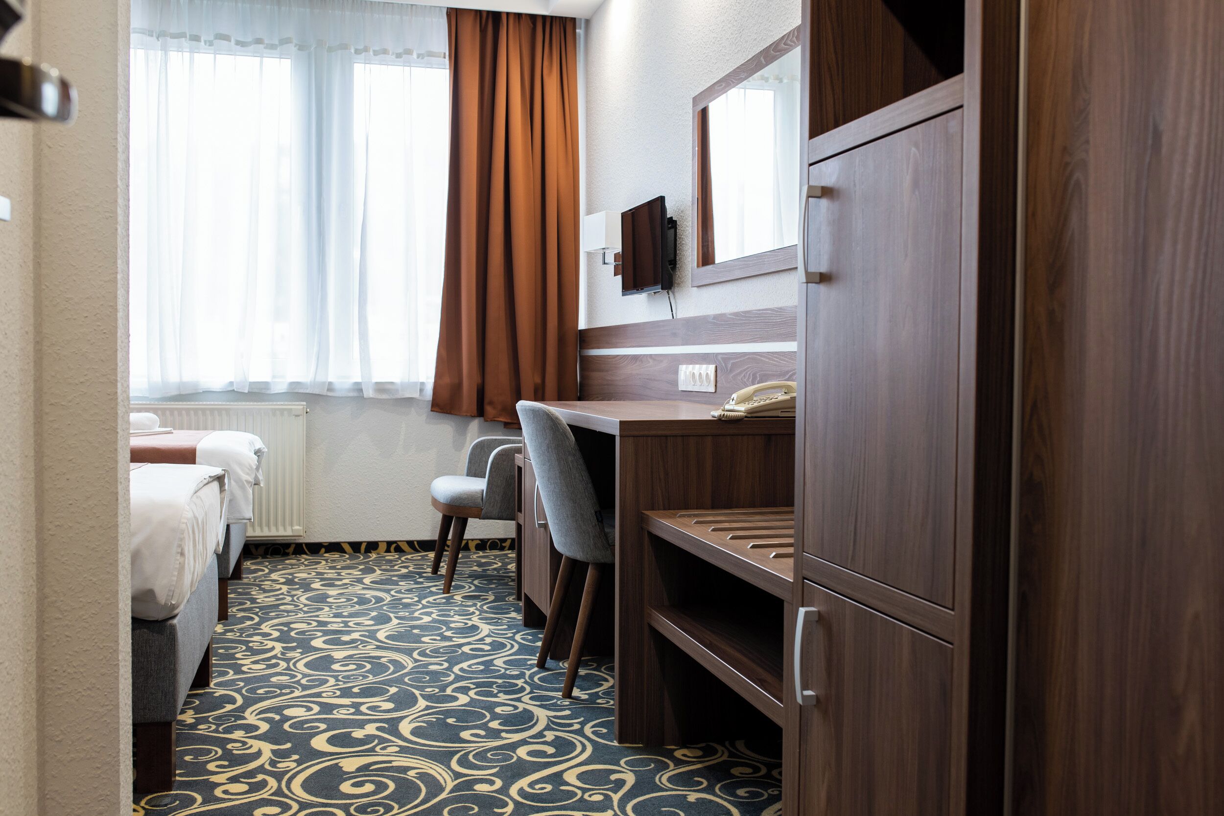 Quarto de hotel com cama, escrivaninha, cadeira, telefone e espelho.