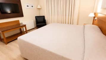 Quarto de hotel com cama, televisão presa na parede, escrivaninha e uma cadeira.