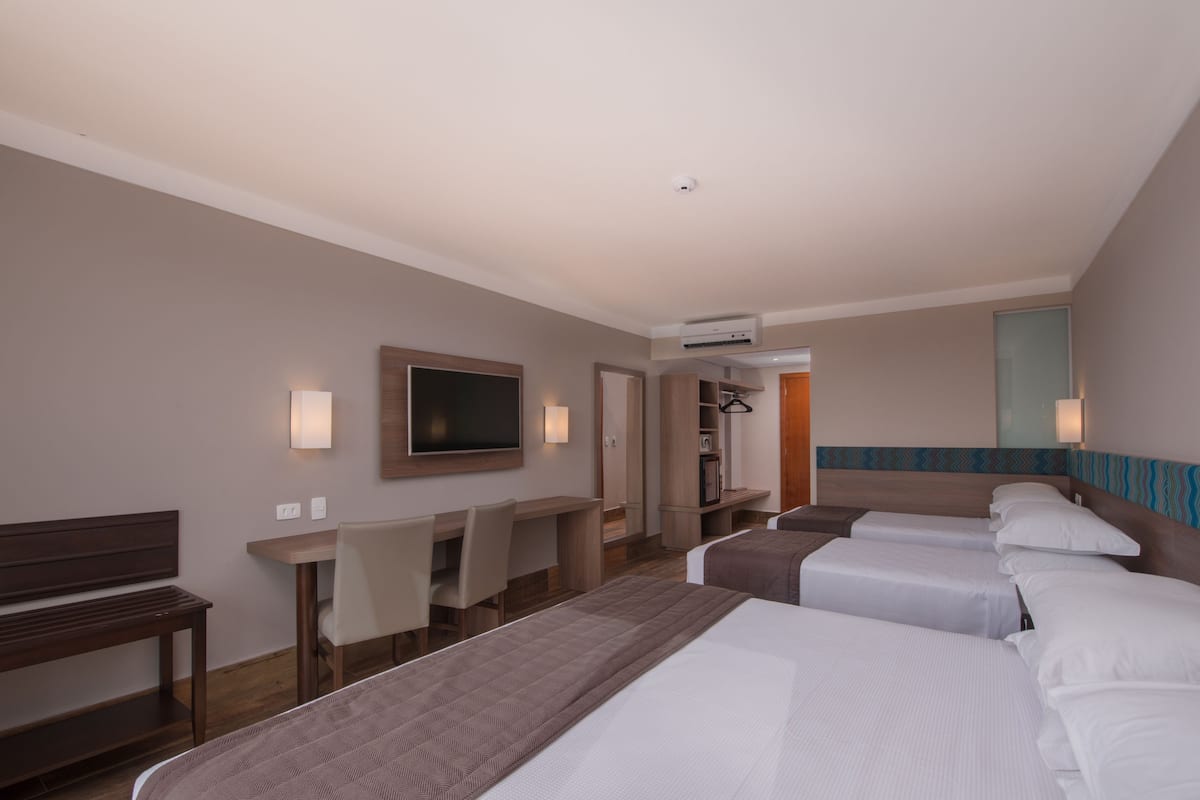 Quarto de hotel com cama grande, escrivaninha, cadeira e televisão.