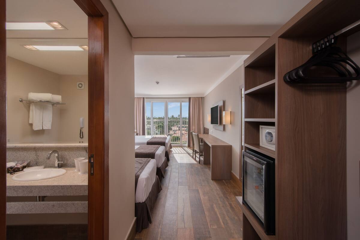 Quarto de hotel com banheiro, duas camas, uma escrivaninha, televisão e vista para o exterior.
