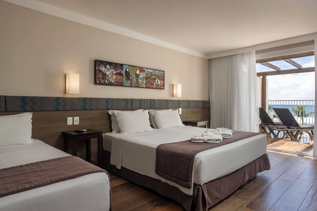 Quarto de hotel com duas camas, um quadro na parede e uma varanda com vista.