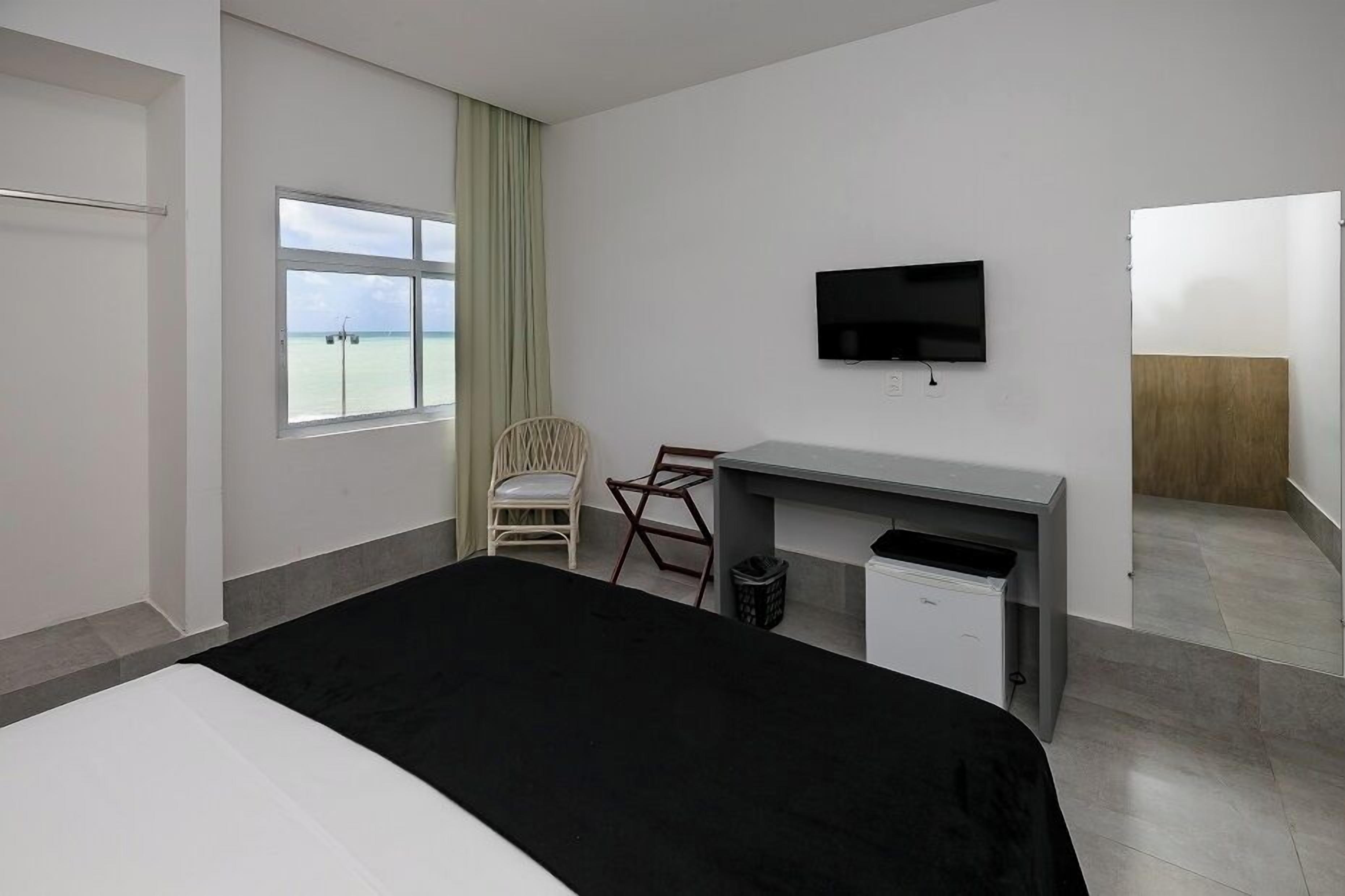 Quarto de hotel com cama, secretária, cadeira, televisão e janela com vista para o mar.
