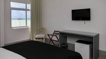 Quarto de hotel com cama, escrivaninha, cadeira, televisão e vista para o mar.