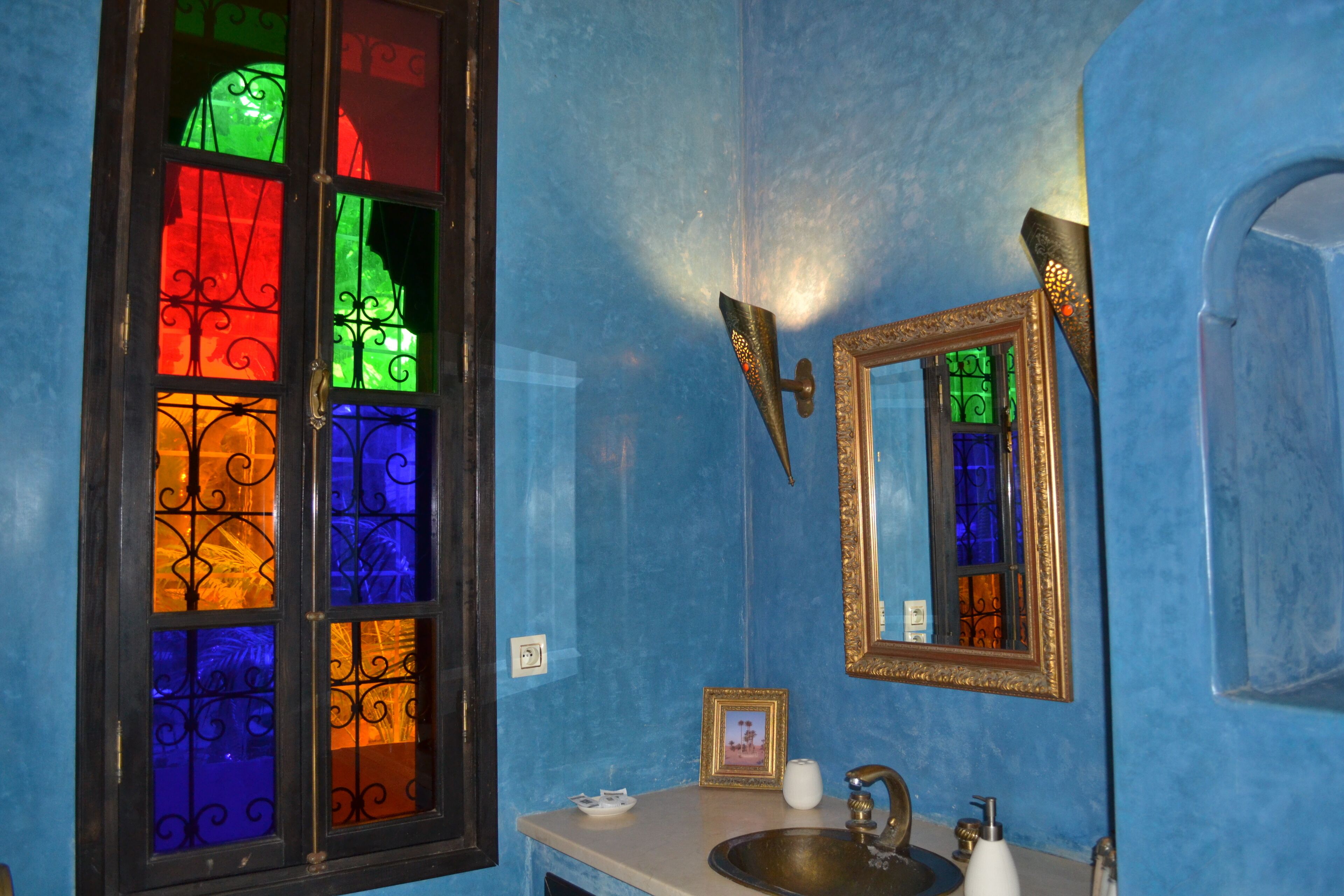 Casa de banho com parede azul, pia, espelho e janelas de vitrais.