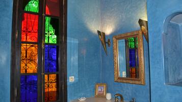 Casa de banho com parede azul, pia, espelho e janelas de vitrais.