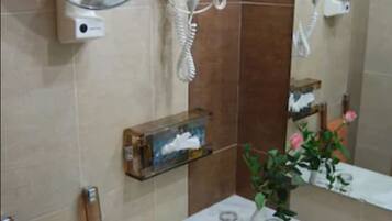 Uma casa de banho com uma pia branca, um espelho redondo e dois secadores de cabelo fixados na parede.