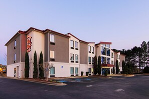 Um hotel de vários andares com telhado plano, janelas amplas e um estacionamento na frente.