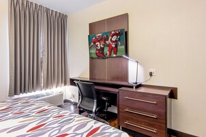 Quarto de hotel com cama, escrivaninha, cadeira, cômoda e um quadro na parede.