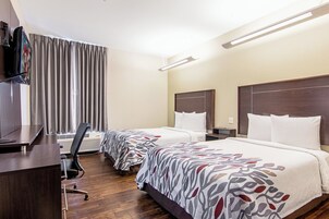 Quarto de hotel com duas camas, uma escrivaninha, uma televisão e uma cadeira.