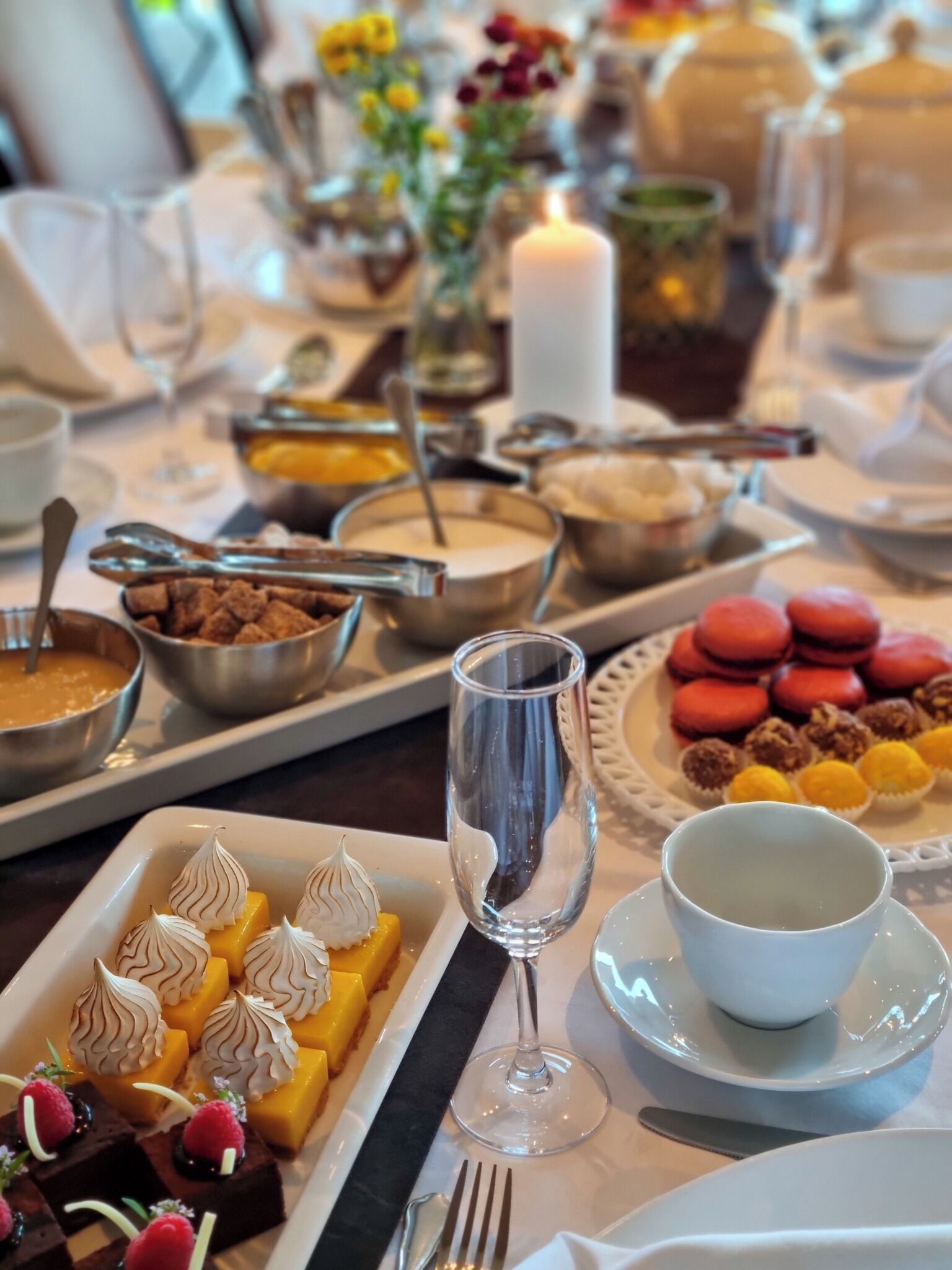 Uma mesa de jantar posta com diversos pratos, incluindo macarons, um copo de água e uma bandeja de sobremesas com merengues e frutas vermelhas.