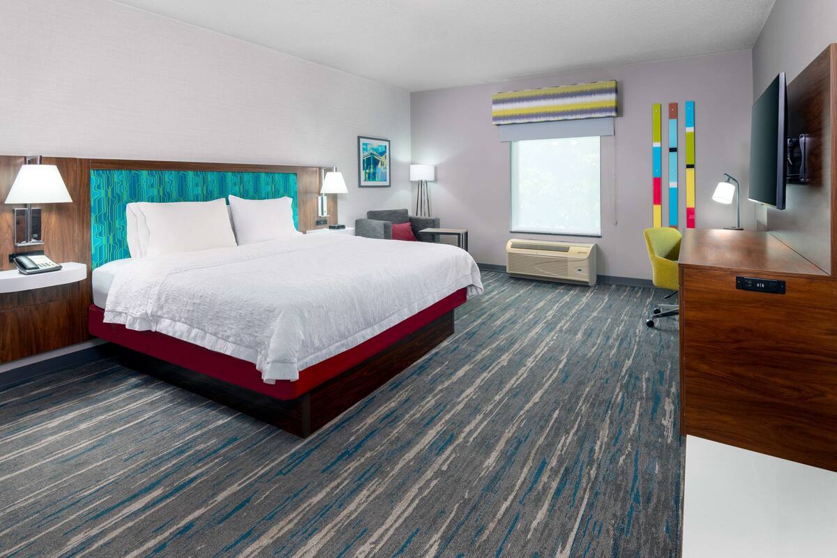 Quarto de hotel com uma cama grande, uma mesa com cadeira, televisão e janela com vista.