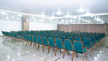 Uma sala de conferências com fileiras de cadeiras cor de verde-água e um palco com cortina.