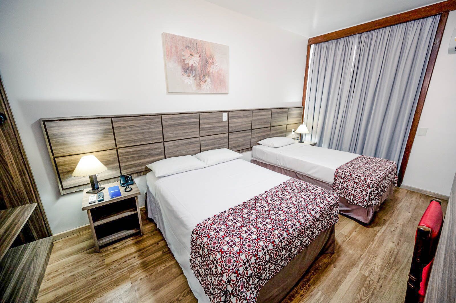 Quarto de hotel com duas camas, uma mesa de cabeceira com abajur, um telefone e uma pequena mesa também com abajur.