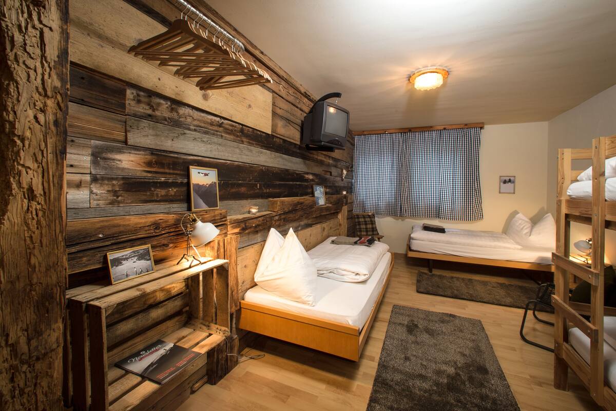 Um quarto rústico com paredes de madeira, uma cama beliche, uma cama de solteiro, uma televisão e uma janela com cortinas xadrez.