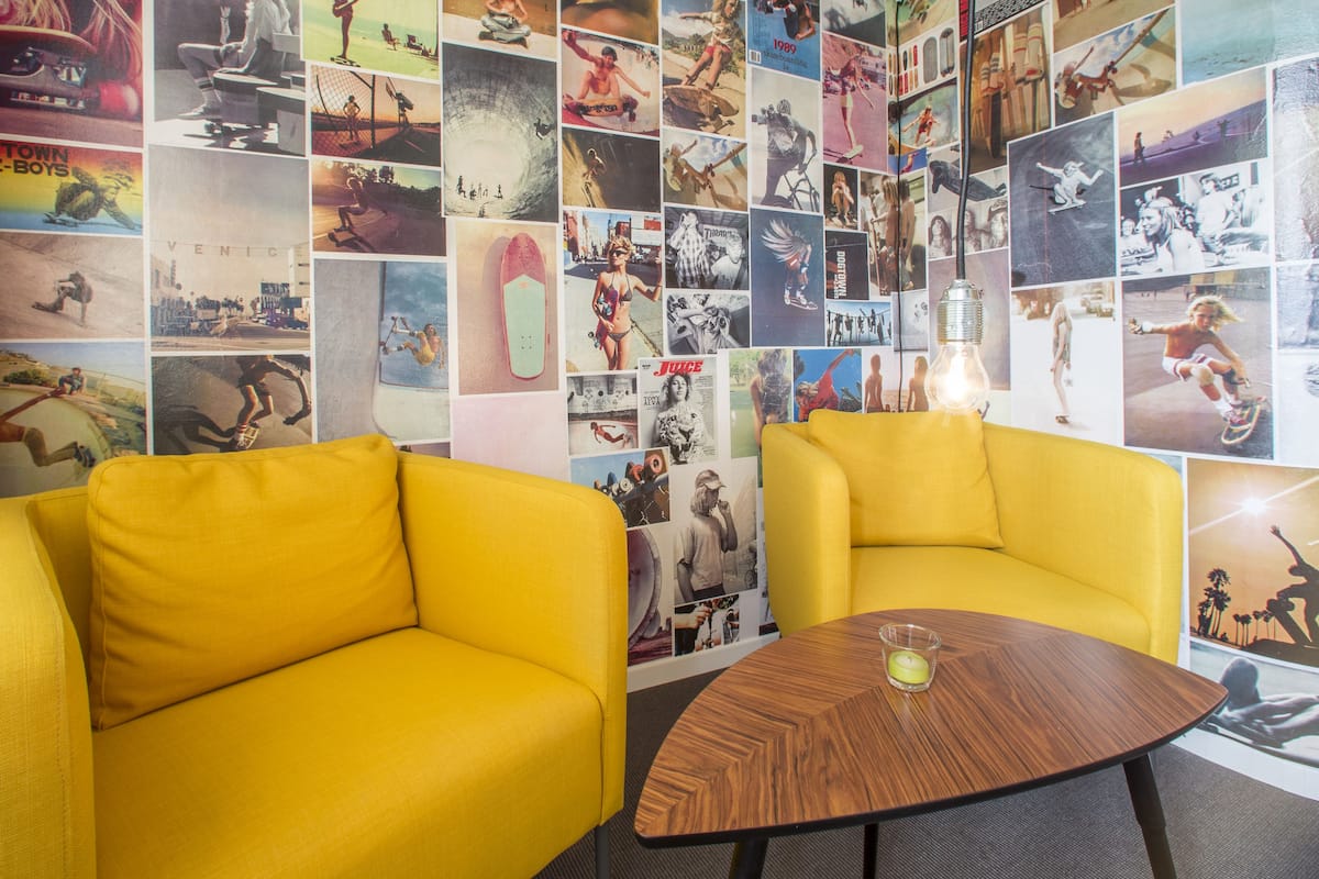 Quarto com sofás amarelos, uma mesa de madeira e uma parede decorada com diversas fotografias.