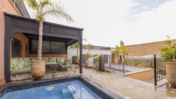 Área de piscina no terraço com espaço para sentar, pérgola e vasos de plantas.