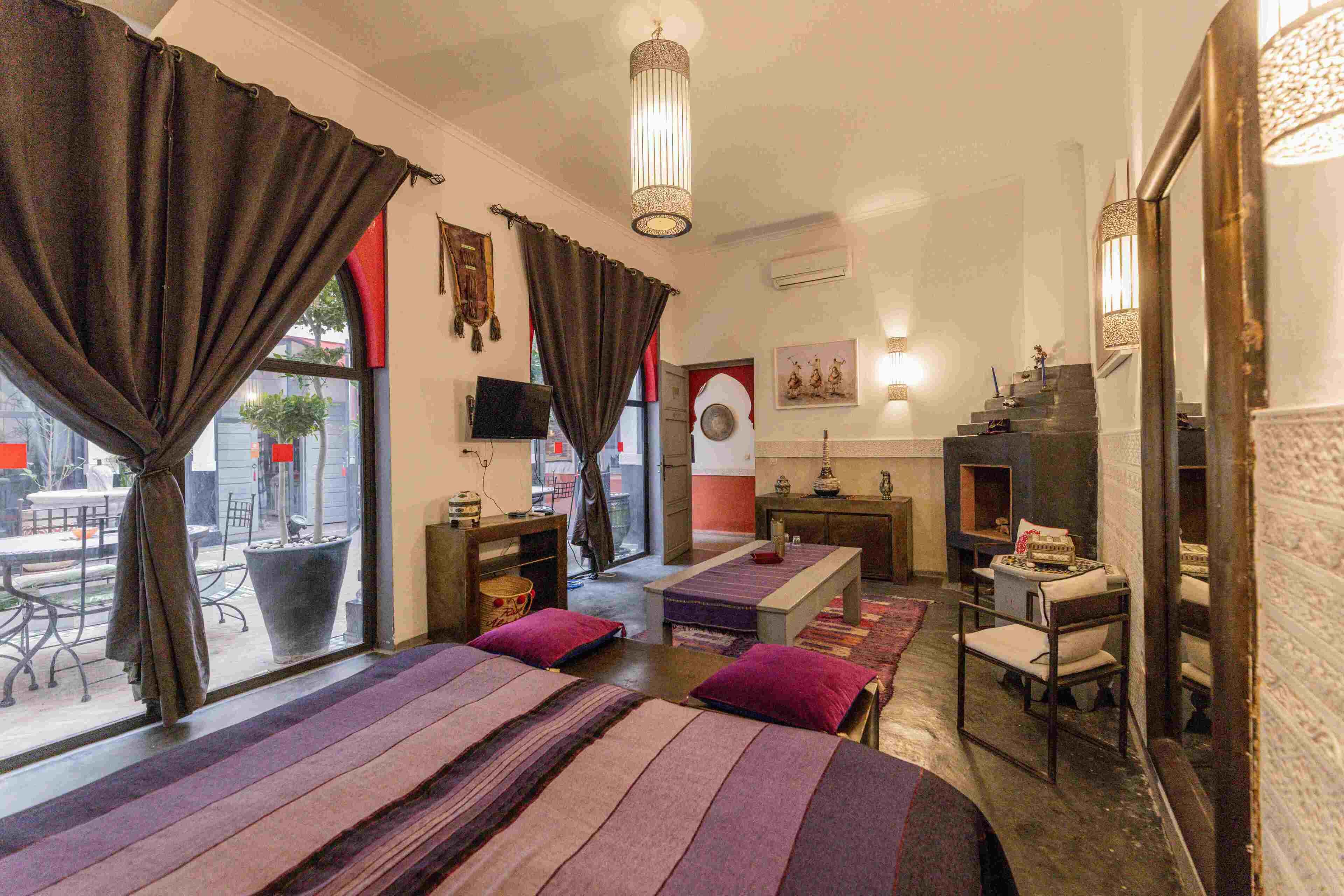Quarto de hotel com uma cama grande, escrivaninha, cadeira, lareira e vista para a rua.