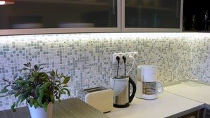 Uma cozinha com bancada branca, torradeira, cafeteira e um vaso com planta.