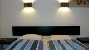 Quarto de hotel com duas camas, cada uma com roupa de cama listrada, cabeceira preta e duas mesas de cabeceira com luminárias.