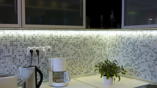 Uma cozinha com painel de azulejos, cafeteira, torradeira e uma planta.