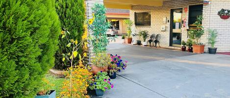 Entrada de hotel com fachada de tijolos, plantas em vasos e área de estar externa.