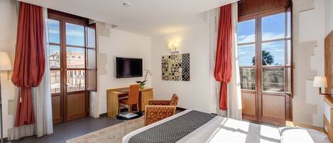 Quarto de hotel com cama, escrivaninha, cadeira, TV e janelas amplas com cortinas.