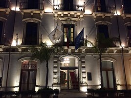 Um edifício histórico com uma entrada imponente, várias bandeiras e uma escadaria que leva à entrada.