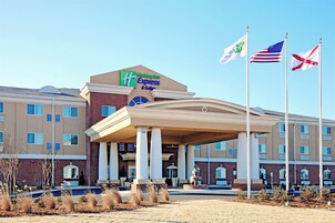 Um hotel Holiday Inn Express & Suites com entrada destacada, várias bandeiras e área ajardinada com uma fonte.