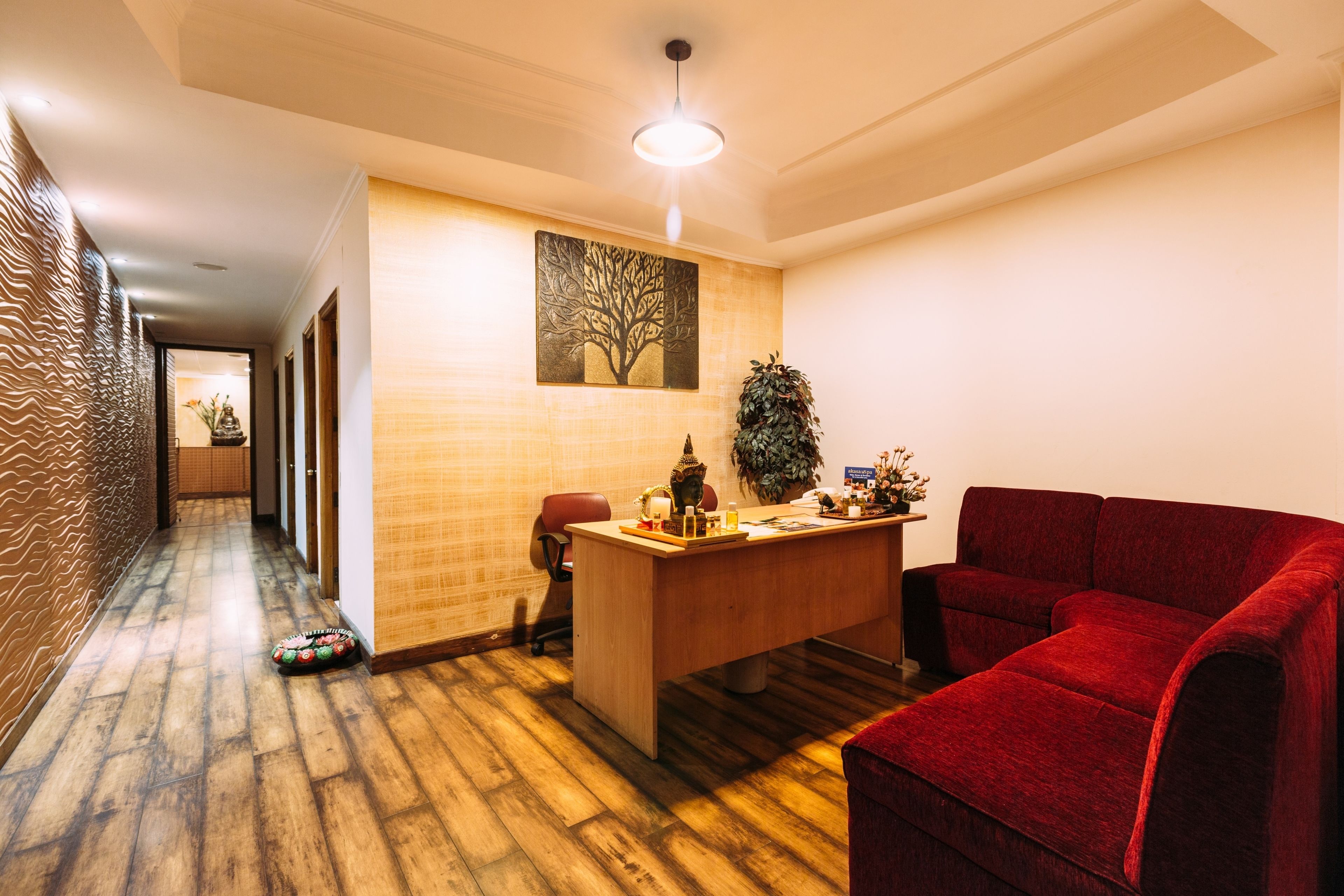 Quarto com chão de madeira, uma escrivaninha com uma planta, um sofá vermelho e uma parede com pintura de árvore.