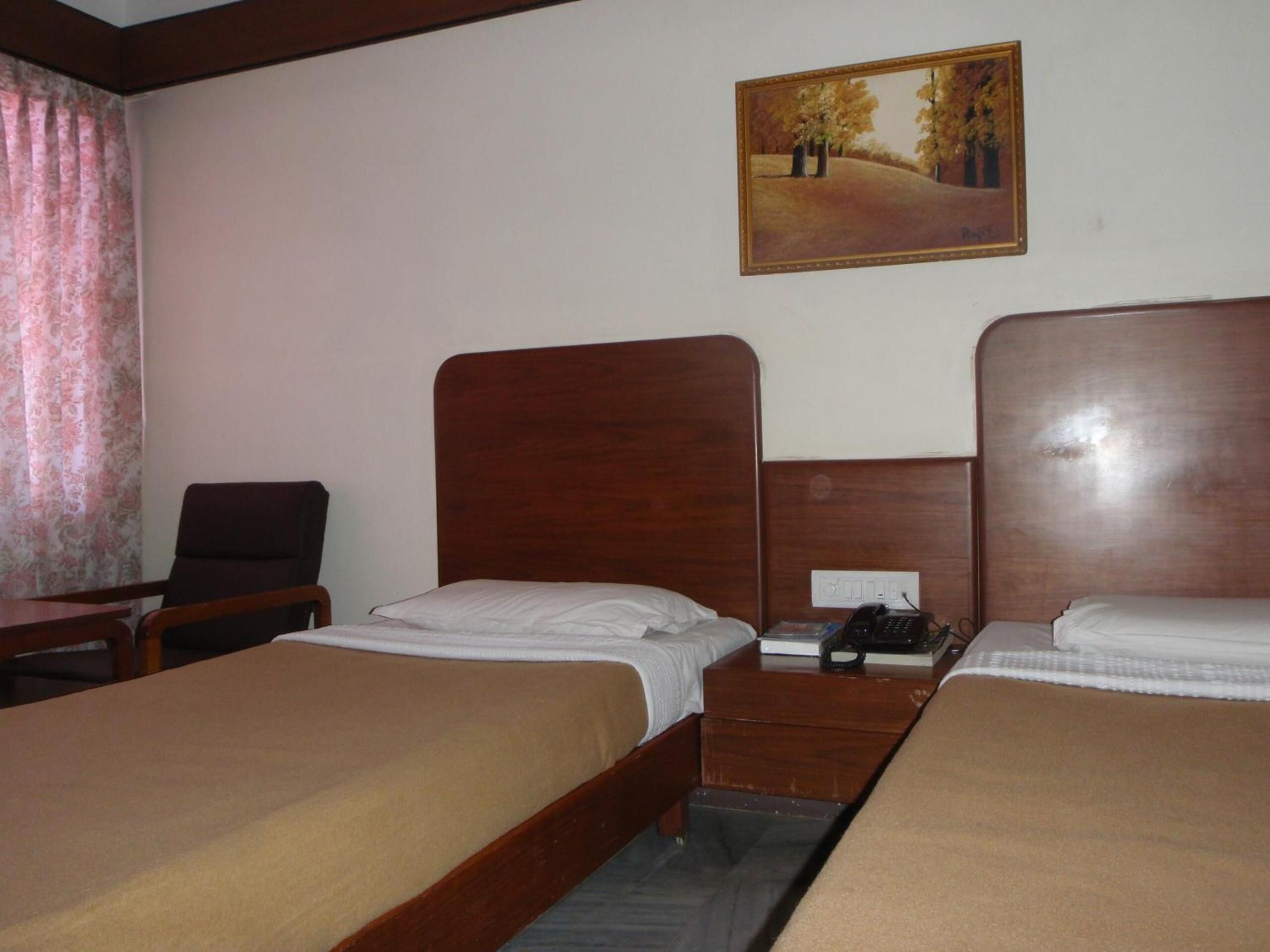 Quarto de hotel com duas camas de madeira, uma escrivaninha, uma cadeira e um quadro na parede.