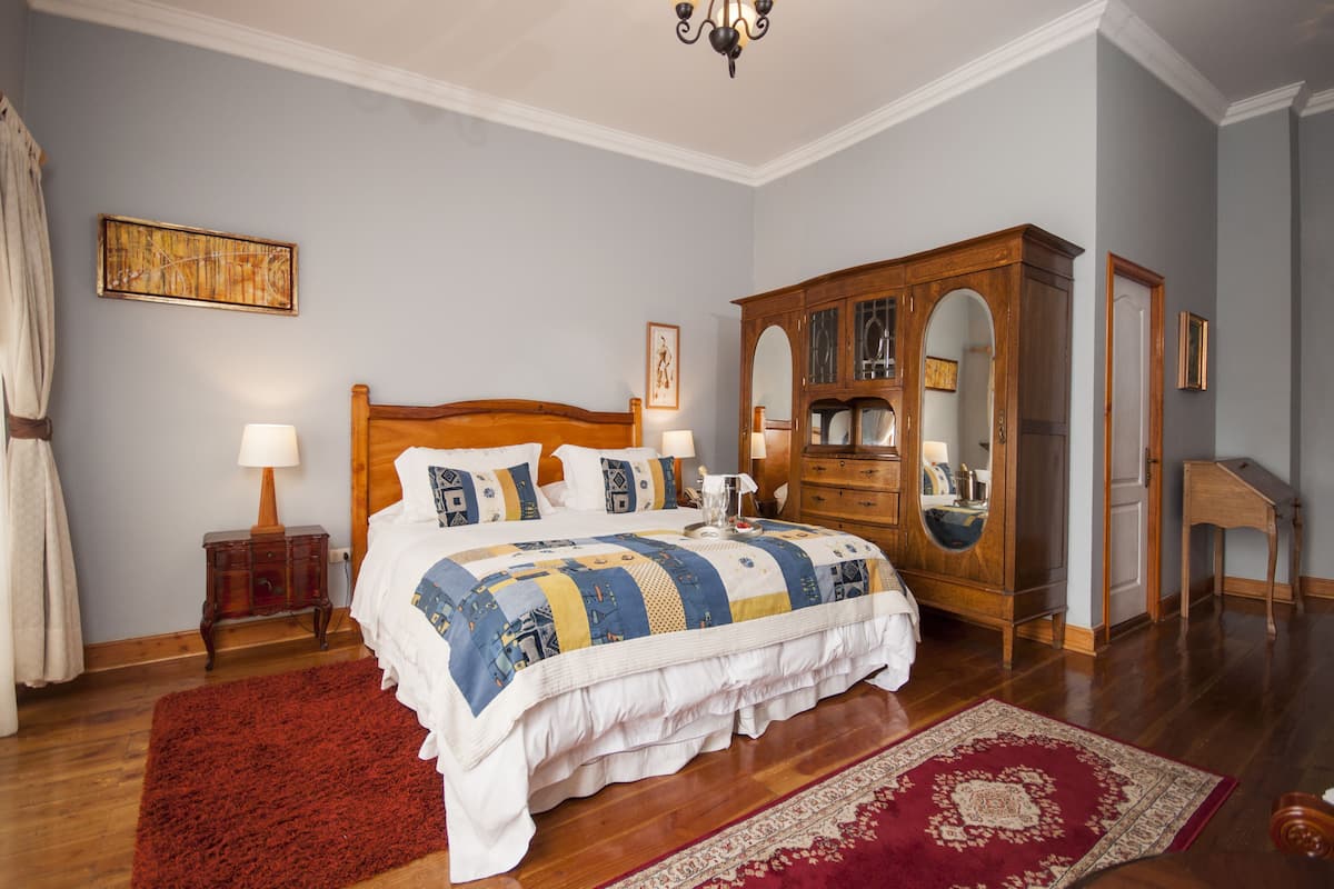 Quarto com cama de madeira, tapete vermelho, cómoda de madeira e espelho.