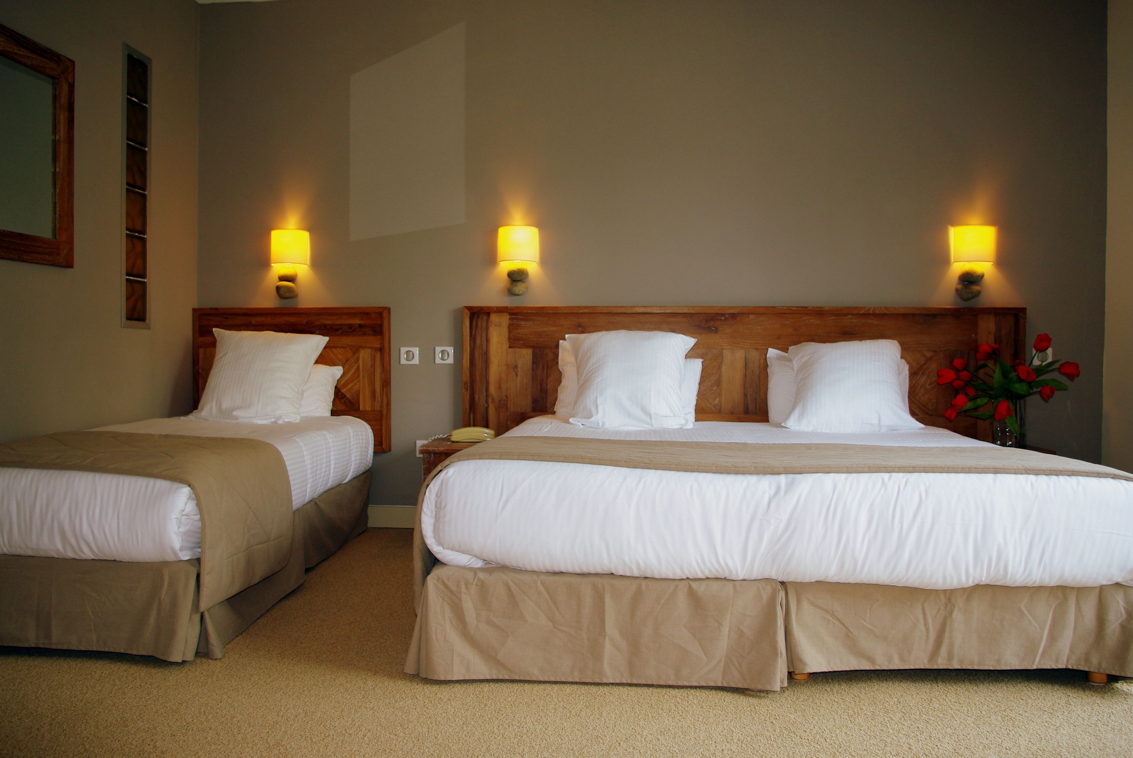 Quarto de hotel com duas camas, roupa de cama bege e luminárias fixadas na parede.