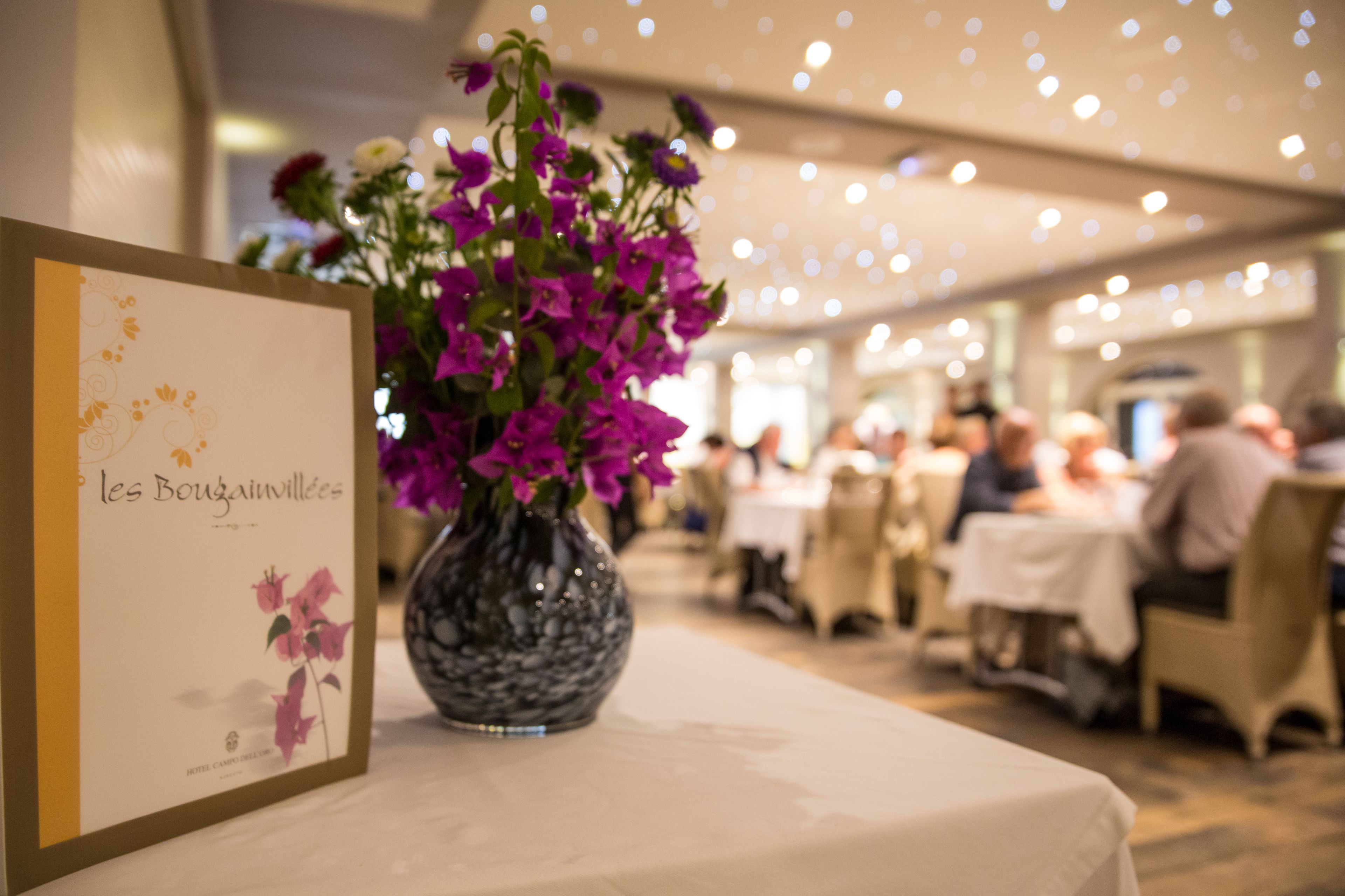 Uma mesa com um menu emoldurado e um vaso de flores roxas em um restaurante.