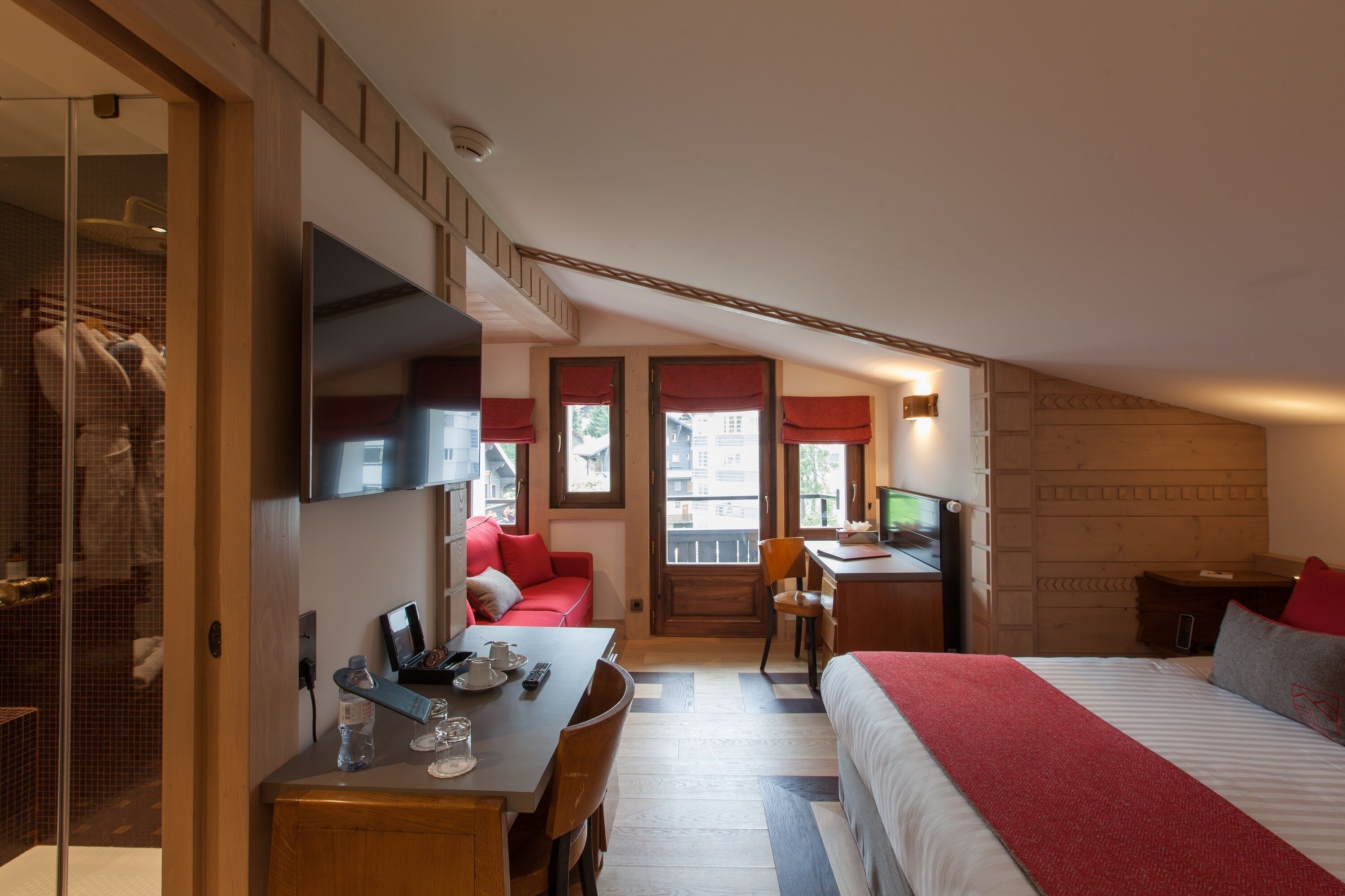 Quarto de hotel moderno com cama, escrivaninha, cadeira, televisão e área de chuveiro.