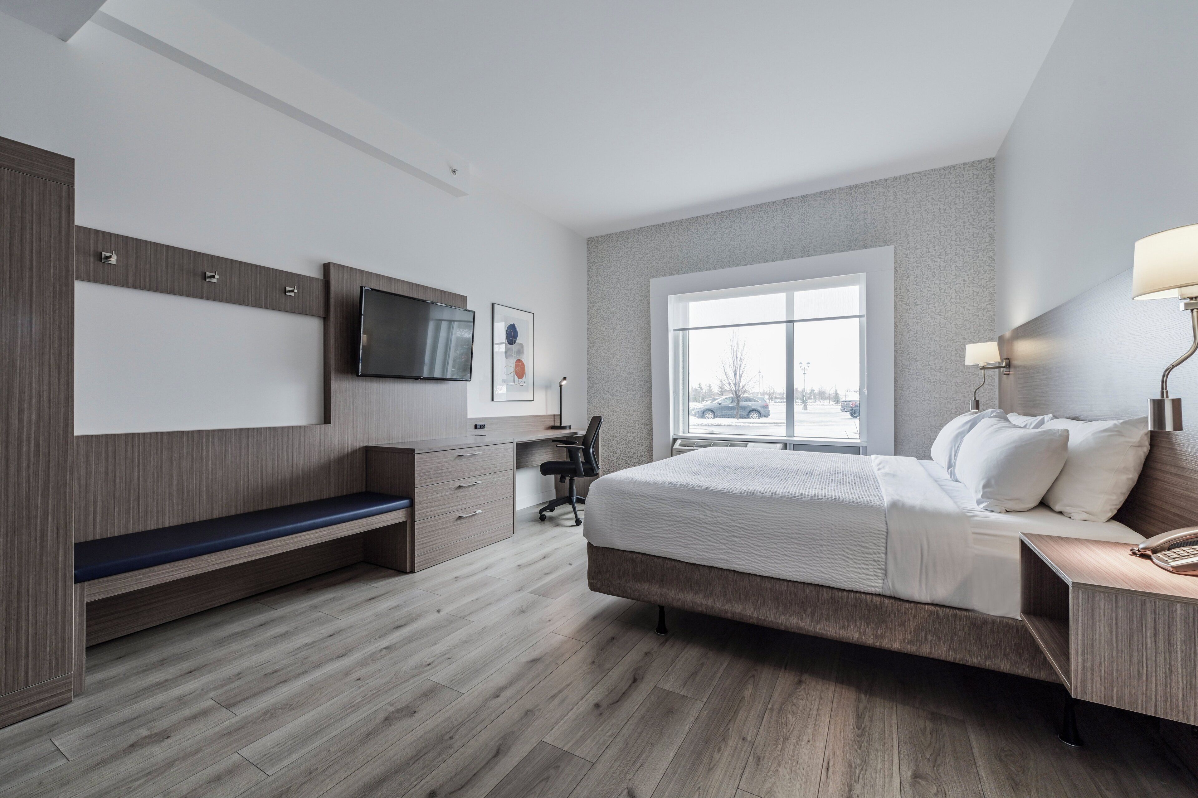 Quarto moderno com cama, escrivaninha, banqueta e televisão.