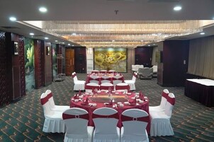 Uma sala de banquetes com mesas redondas, cadeiras brancas e um candelabro.