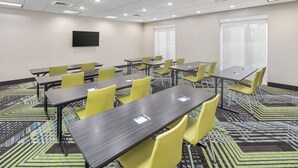 Sala de conferência com várias mesas e cadeiras, uma TV de tela plana na parede e carpete estampado.