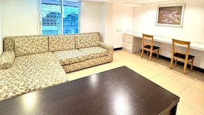 Uma sala de estar com um sofá, uma mesa de centro escura e duas cadeiras de madeira.