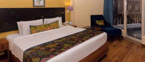 Quarto de hotel com uma cama grande, cabeceira de madeira, mesa de cabeceira, uma cadeira e vista através de uma porta de vidro.