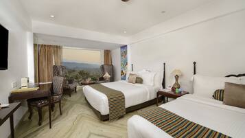Quarto de hotel com duas camas, uma escrivaninha, uma cadeira e uma janela grande com vista.