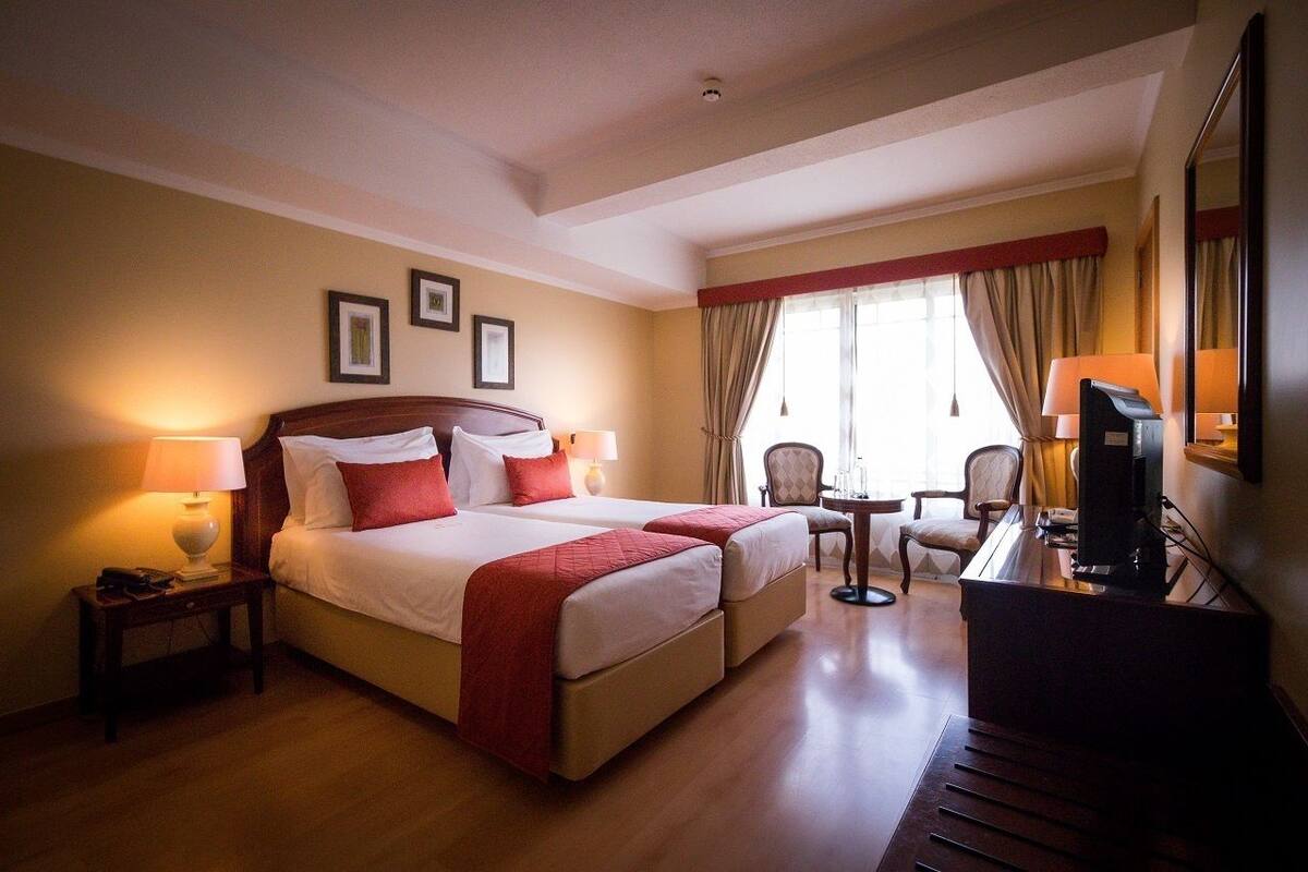 Quarto de hotel com duas camas, uma escrivaninha com computador, uma cadeira e uma televisão.