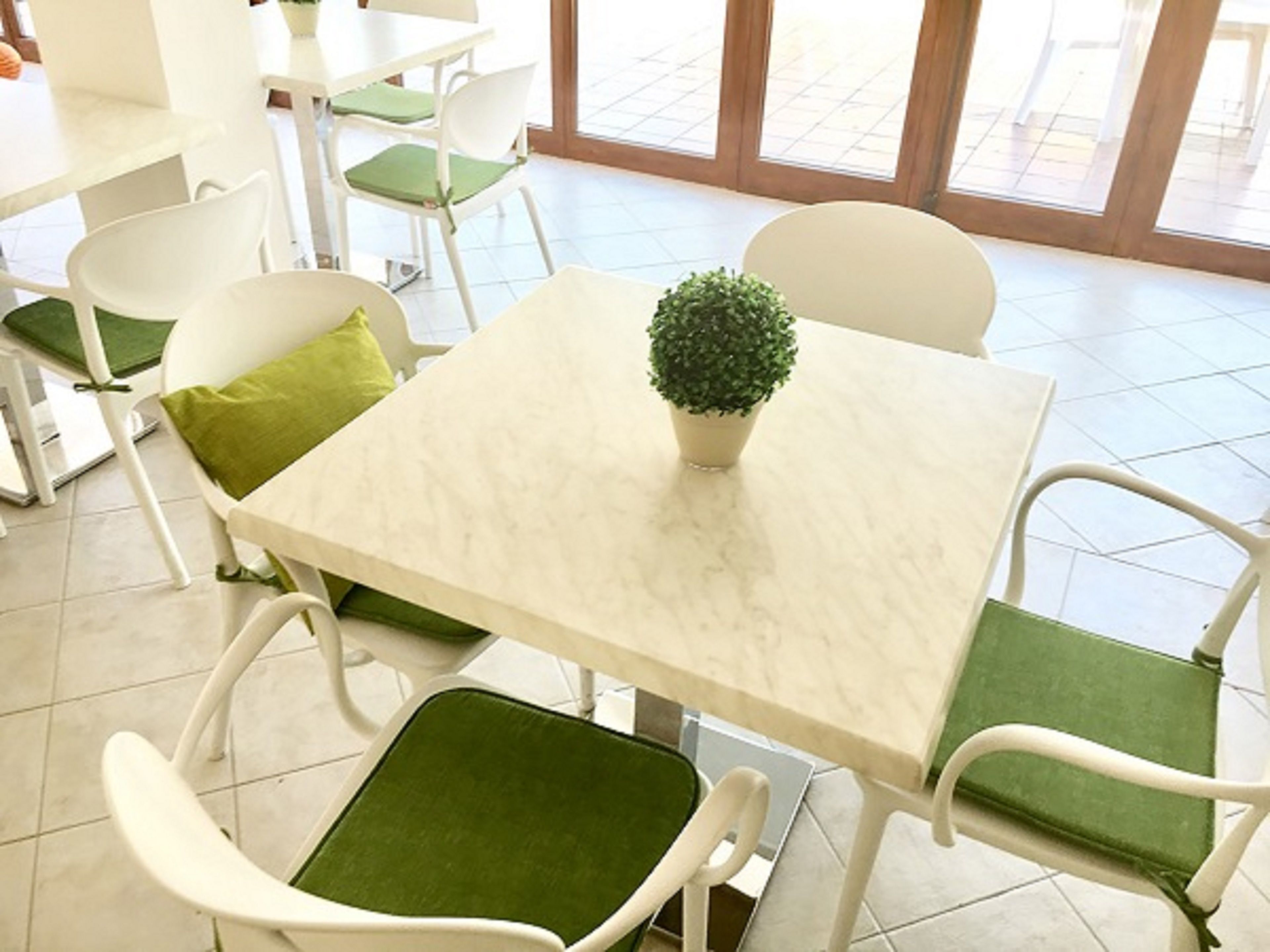 Uma sala de jantar com uma mesa de mármore e cadeiras brancas com almofadas verdes.